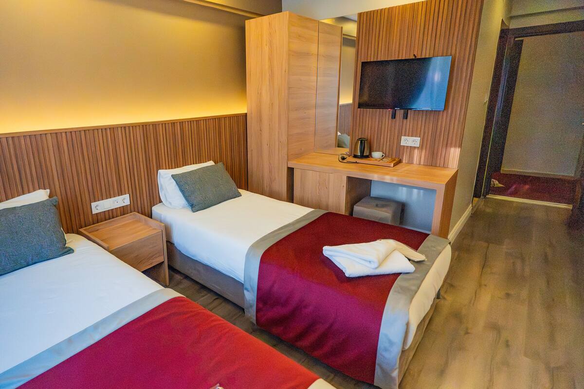 Quarto de hotel com duas camas, cabeceira de madeira, televisão na parede e pequena mesa com cafeteira.