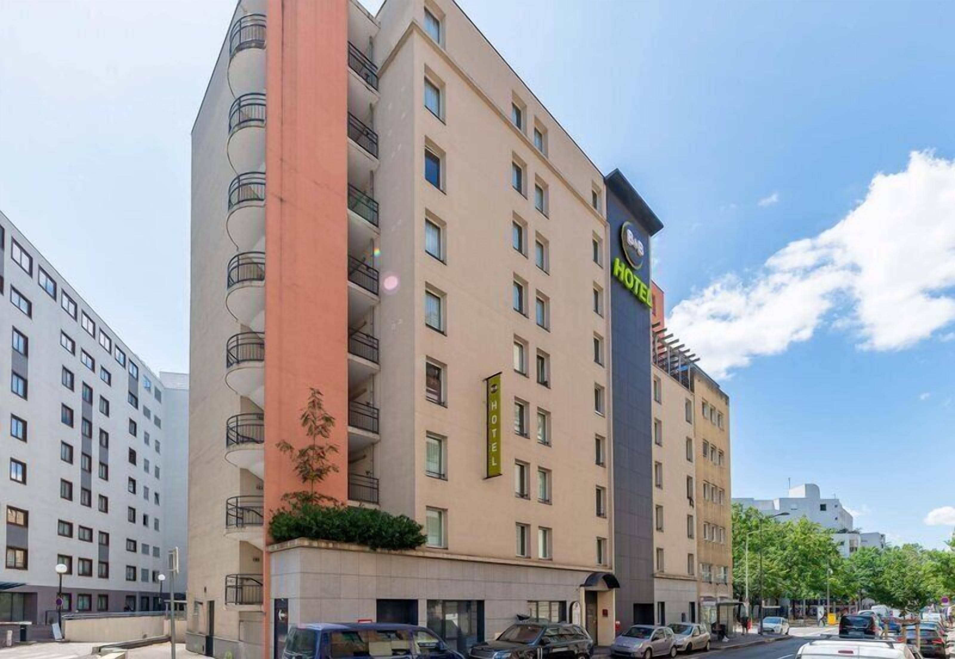 Um hotel com vários andares, um letreiro vertical chamativo, varandas e um estacionamento.