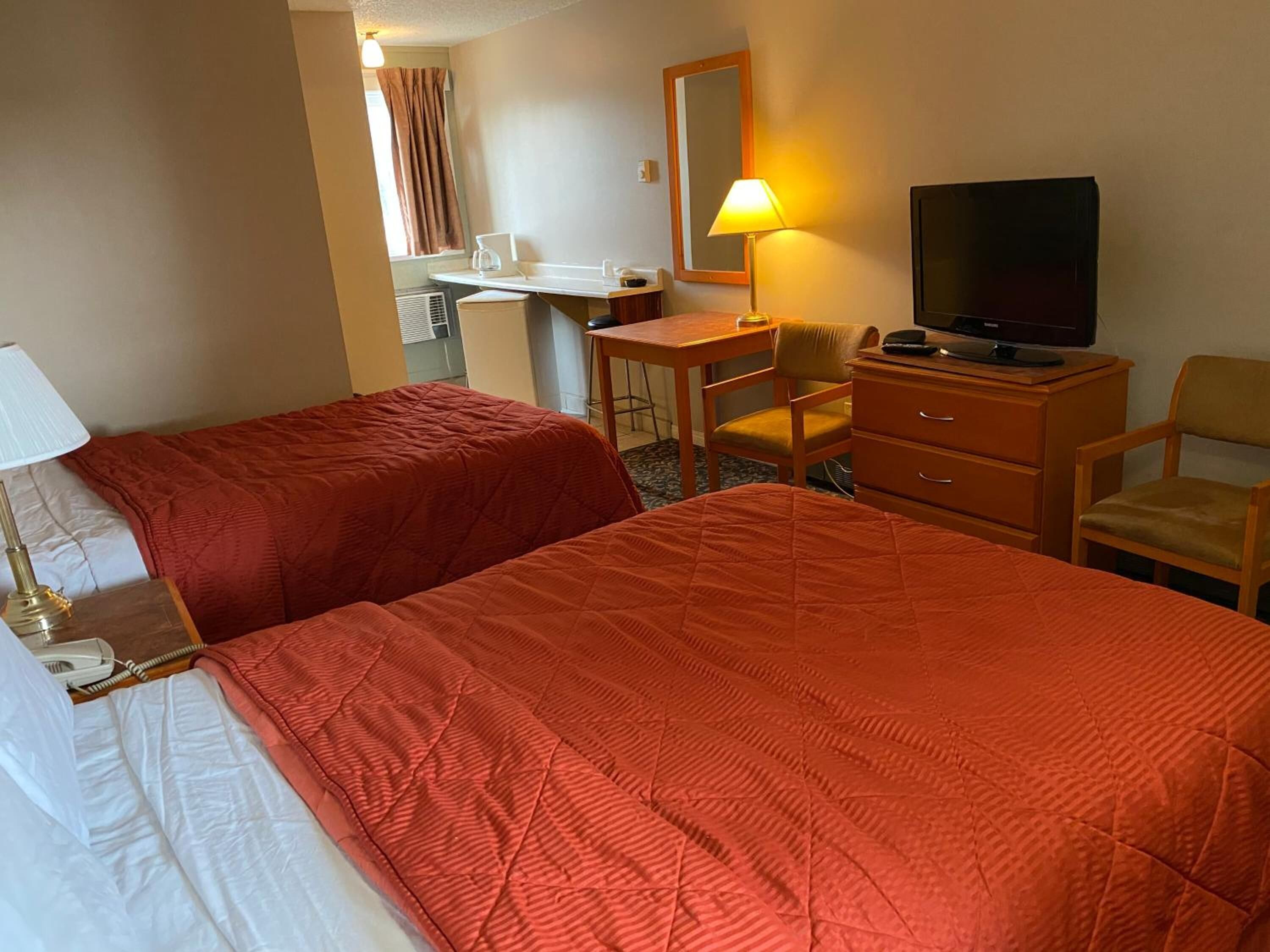 Quarto de hotel com duas camas, uma escrivaninha, uma cadeira, uma televisão e um abajur.