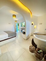 Quarto moderno com cama grande, banheiro com banheira e vista para um jardim exuberante.