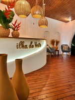 Uma área de recepção com balcão branco curvo, teto de madeira e luminárias de vime pendentes.