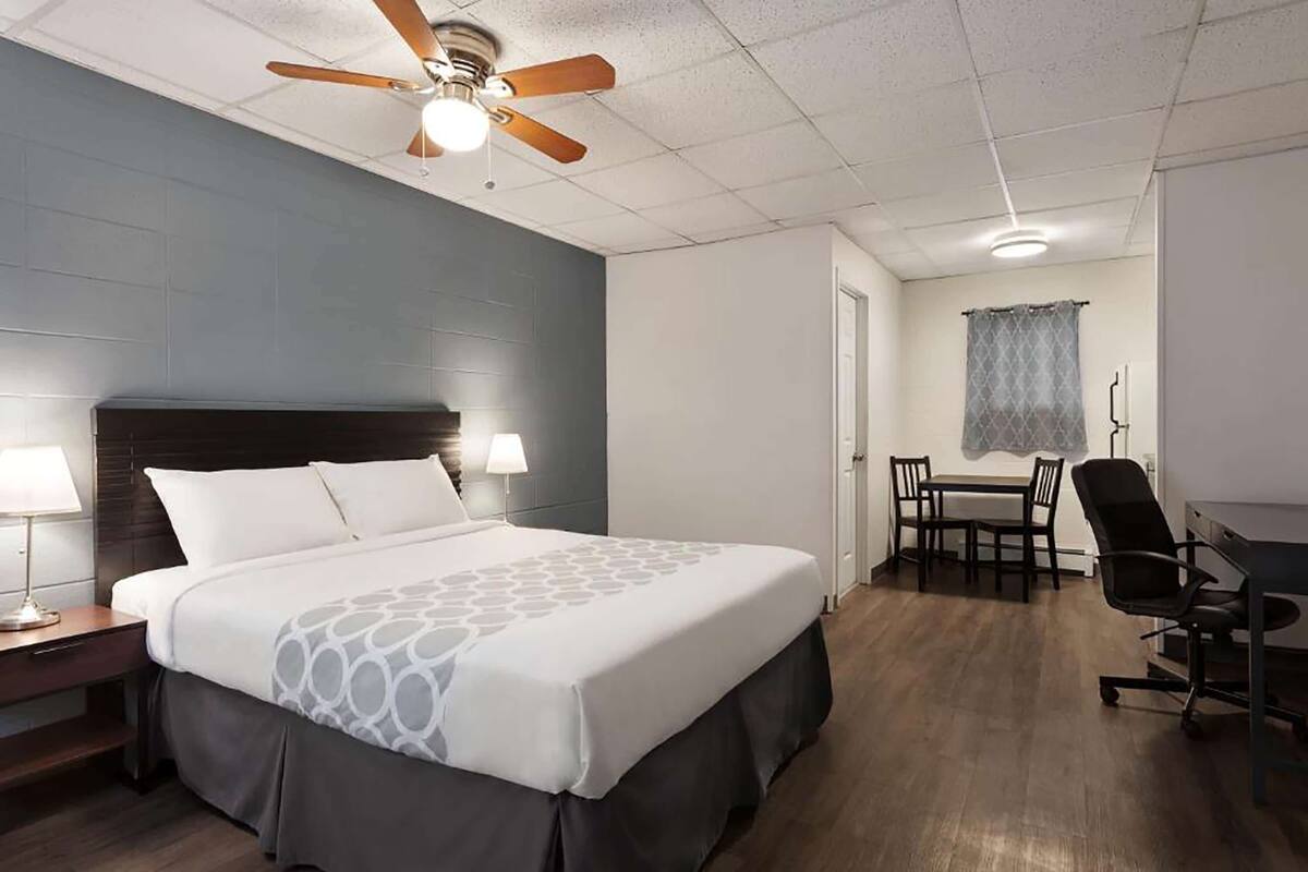 Quarto de hotel com cama, abajures, escrivaninha com cadeira e ventilador de teto.