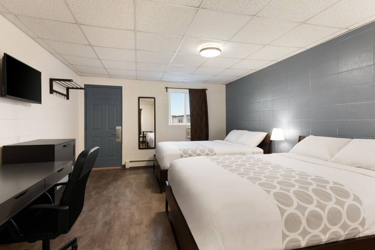 Quarto de hotel com duas camas, uma escrivaninha, uma cadeira, uma televisão e janela com vista para edifícios.