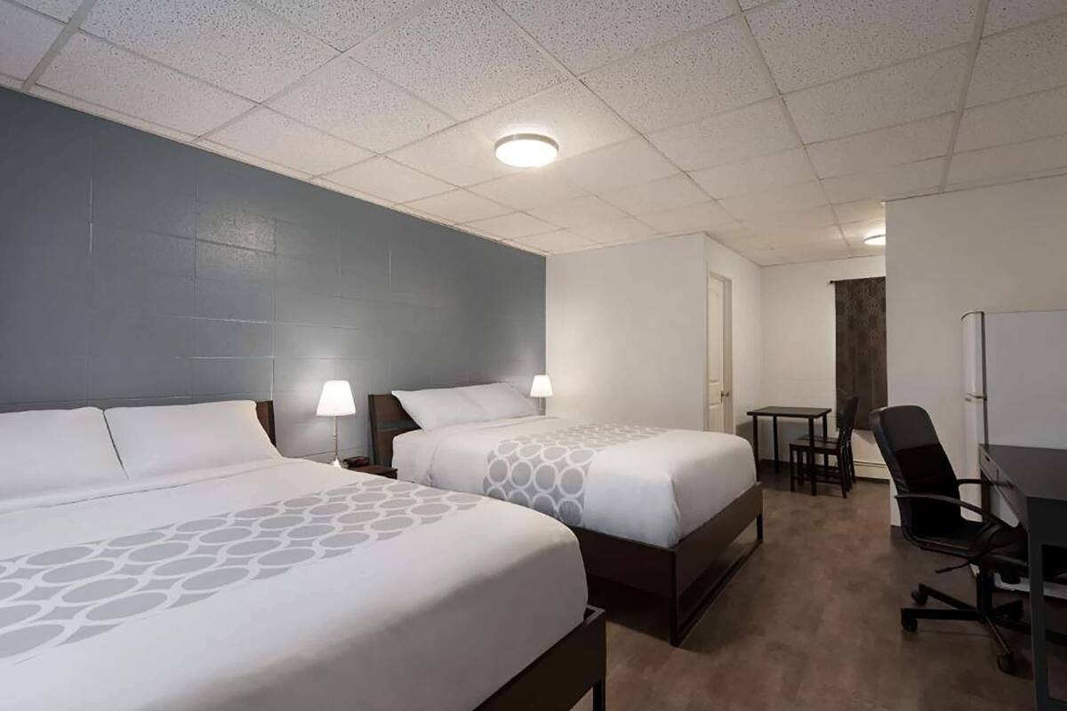 Quarto de hotel com duas camas, uma escrivaninha e uma cadeira.