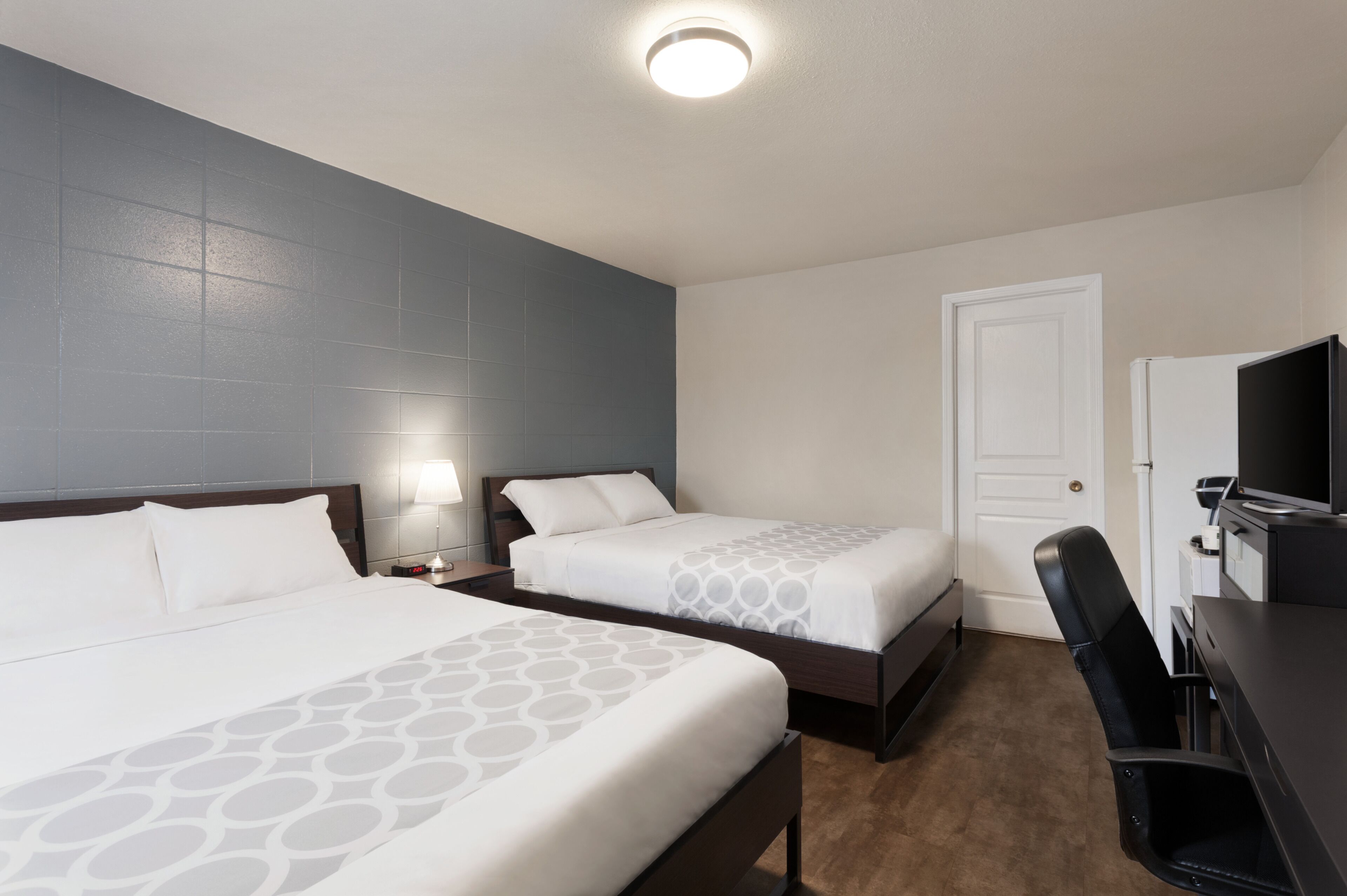Quarto de hotel com duas camas, uma escrivaninha com cadeira, televisão e uma porta.
