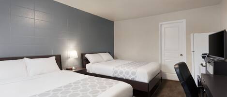 Quarto de hotel com duas camas, uma escrivaninha com cadeira, televisão e uma porta.