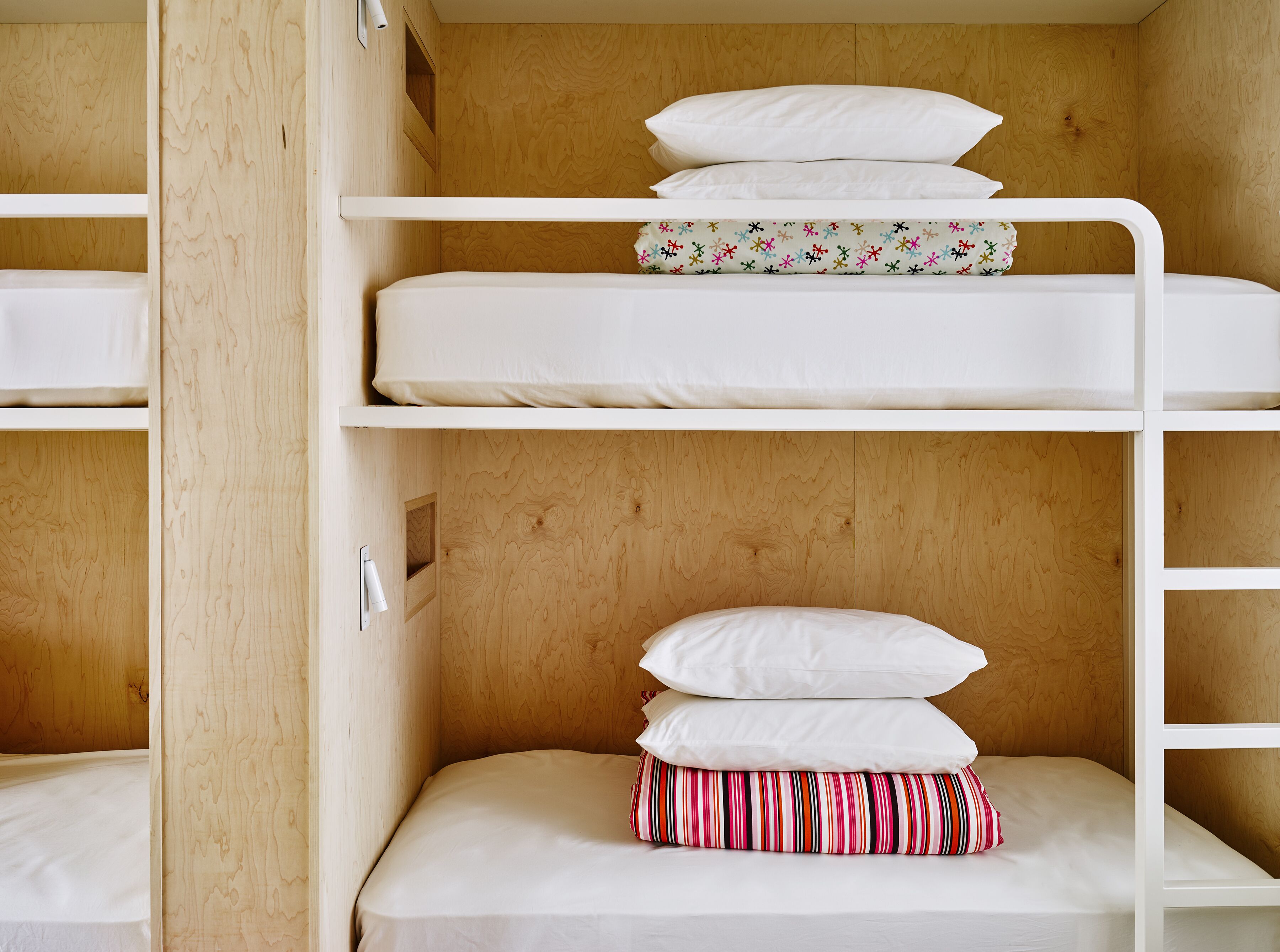 Uma cama beliche com roupa de cama branca e um travesseiro colorido.