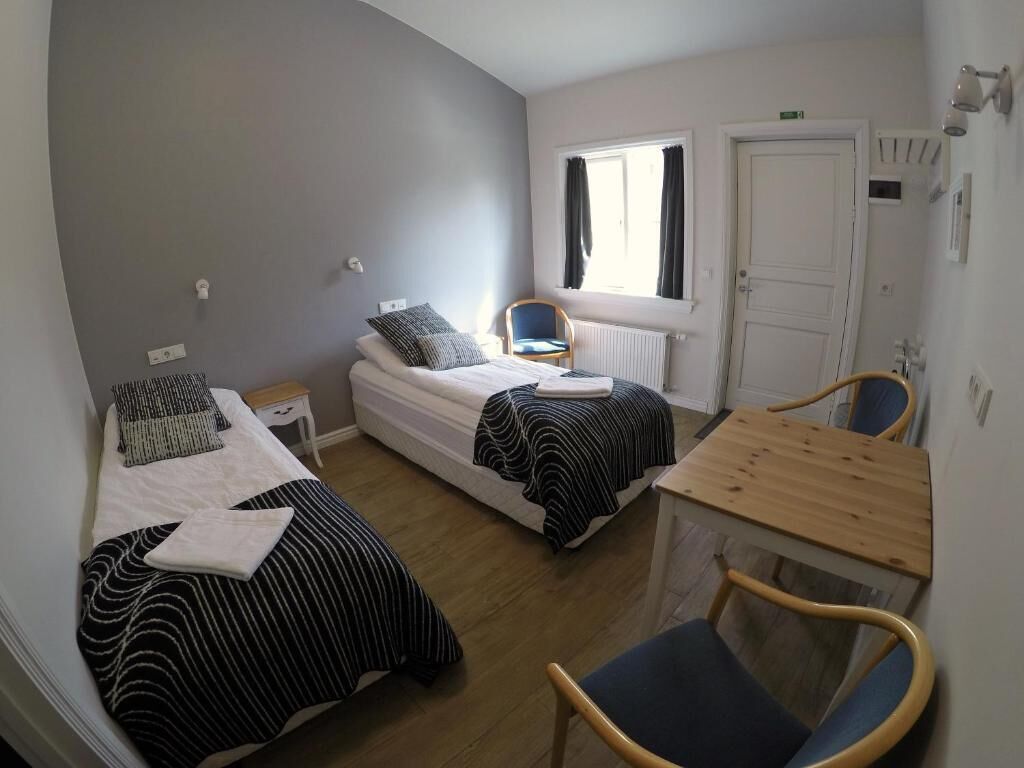 Quarto compacto com duas camas de solteiro, uma mesa pequena e uma cadeira.