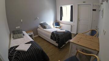 Quarto compacto com duas camas de solteiro, uma mesa pequena e uma cadeira.