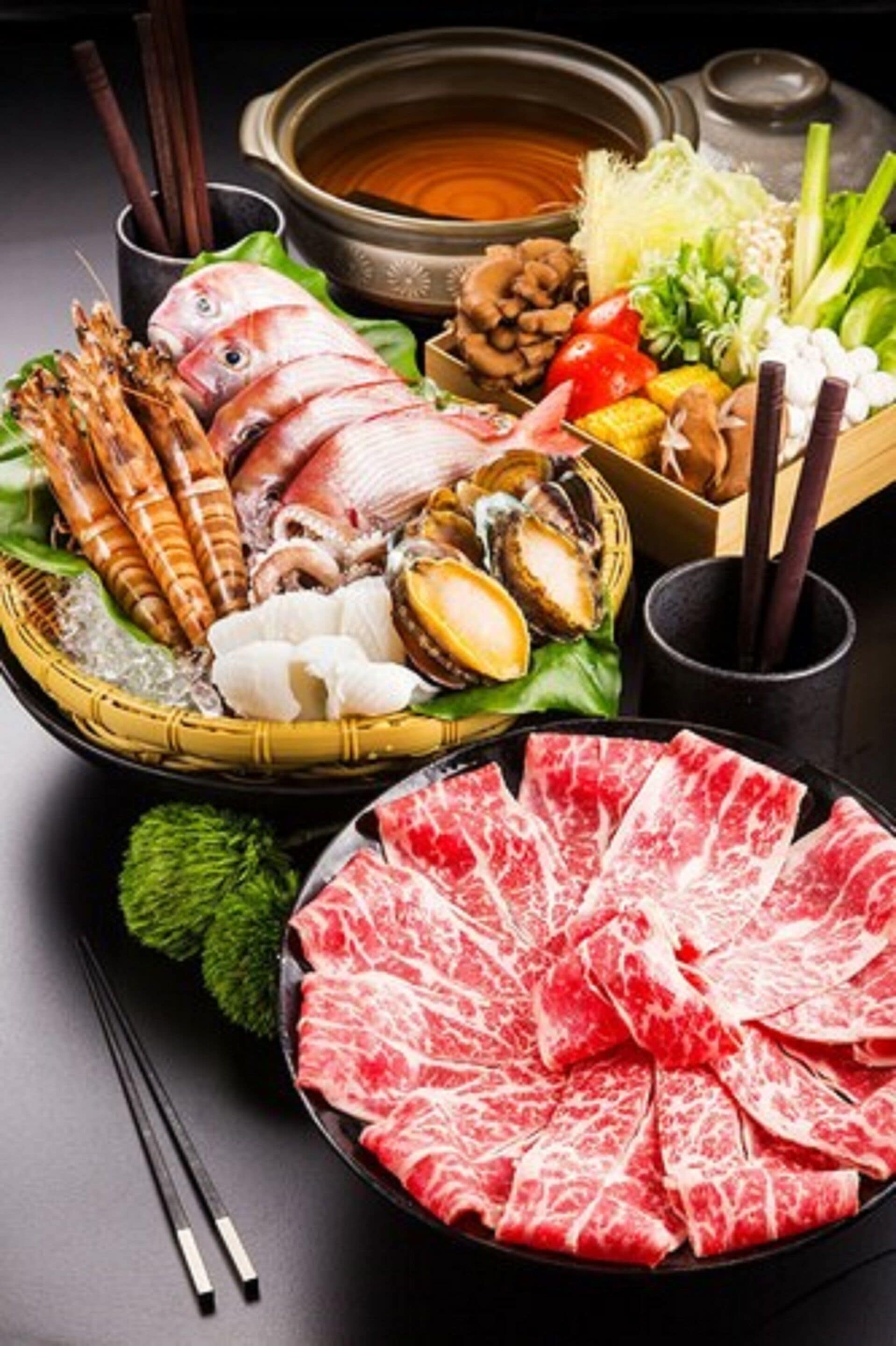 Variedade de frutos do mar, incluindo peixe, camarão e ostras, acompanhada de carne fatiada e legumes.