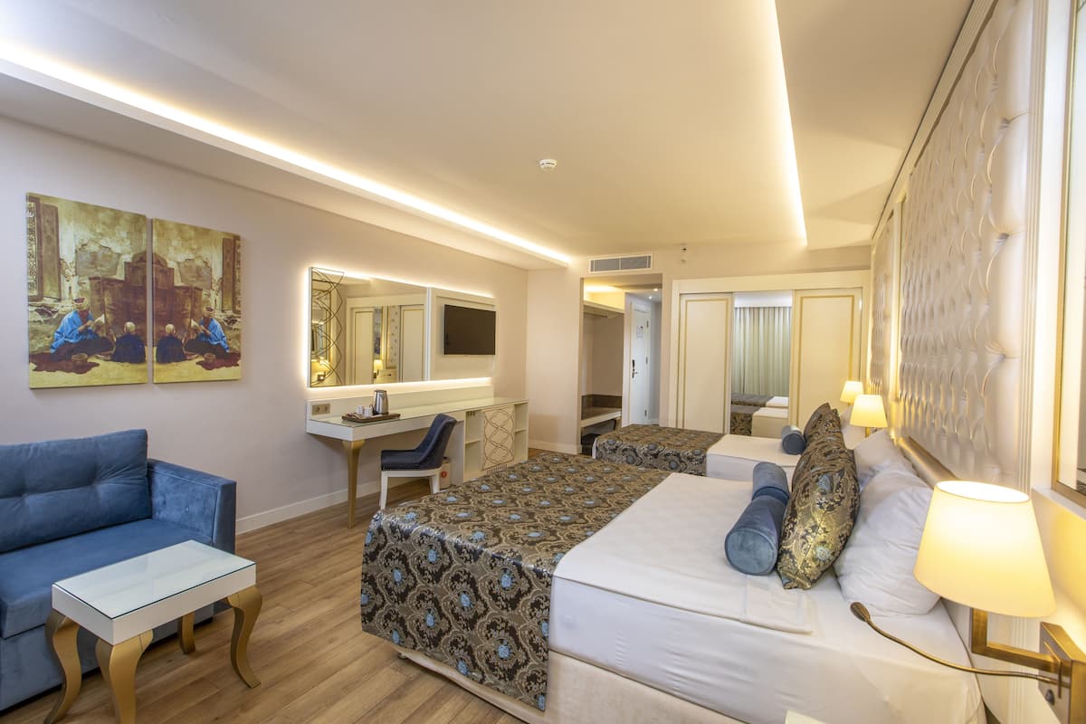 Quarto de hotel com cama, escrivaninha, poltrona, sofá e um espelho grande.