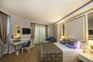 Quarto de hotel com cama, escrivaninha, cadeira, televisão e um espelho grande.
