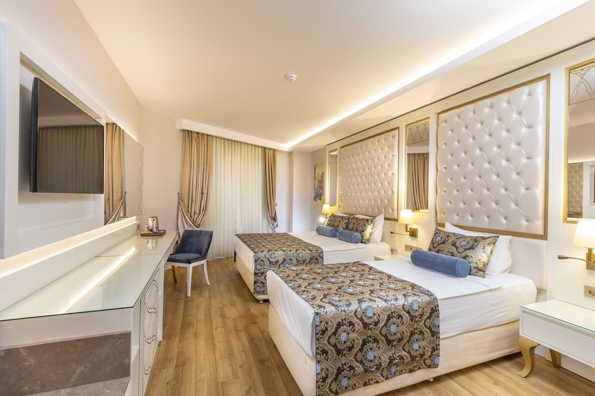 Quarto de hotel com duas camas, área de estar, televisão e mesa de vidro.