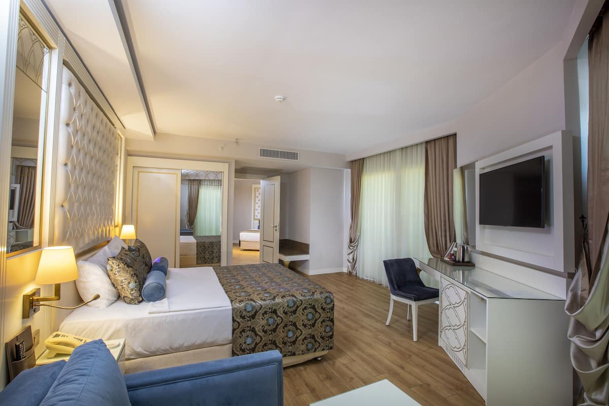 Quarto de hotel com cama, escrivaninha com televisão, cadeira e mesa de cabeceira com abajur.