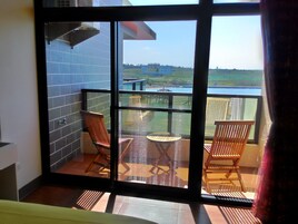Varanda com duas cadeiras de madeira e uma mesa pequena, com vista para um corpo de água e edifícios ao longe.