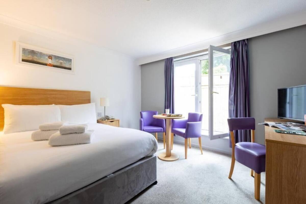 Quarto de hotel com cama, escrivaninha, televisão e janela com cortinas.