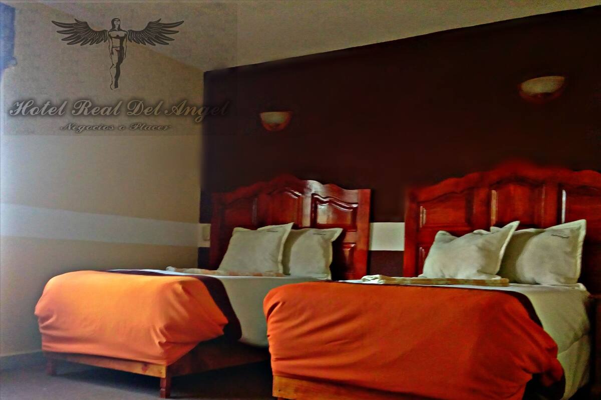 Quarto de hotel com duas camas, cada uma com cabeceira de madeira e roupa de cama branca.