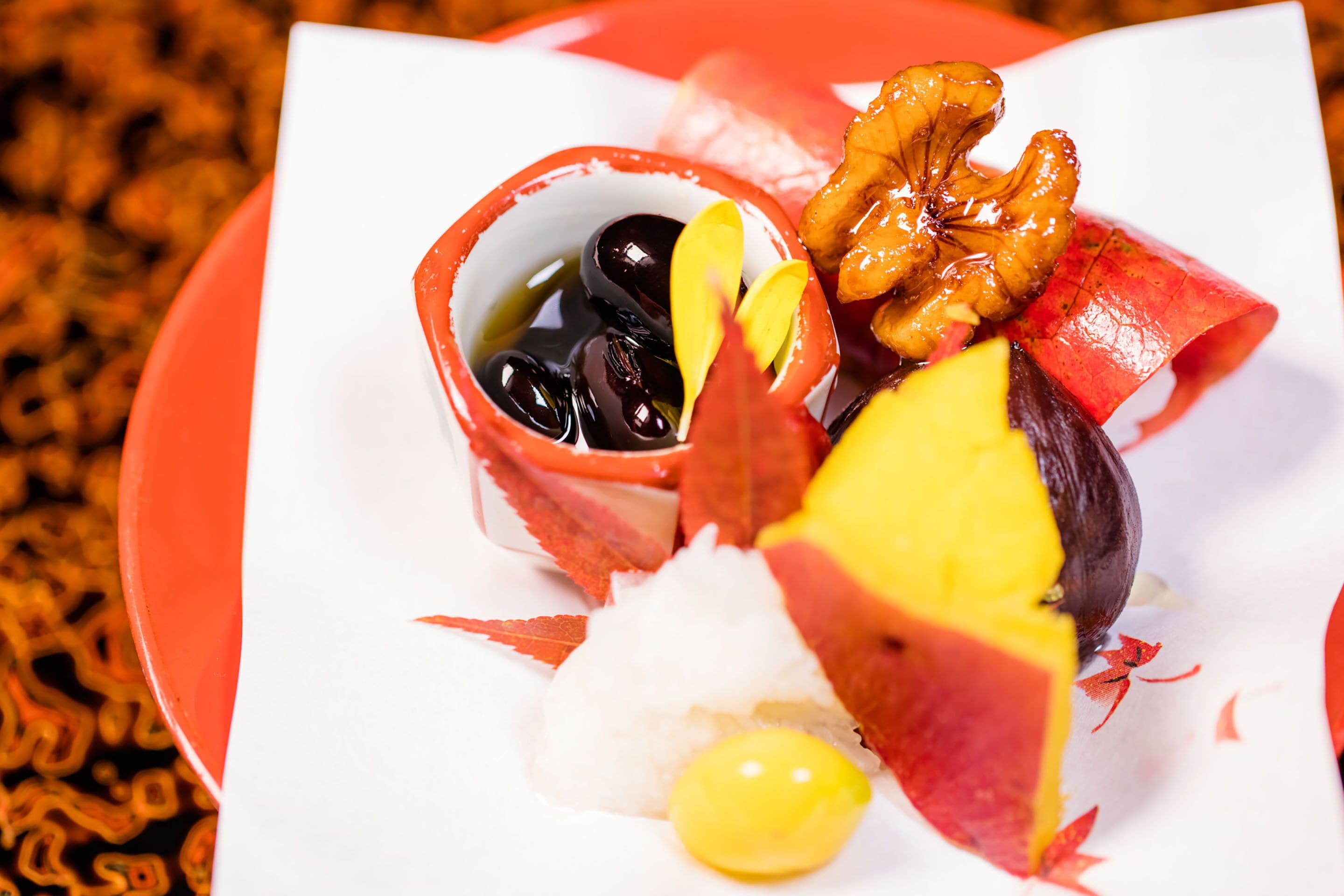 Um prato com diversos alimentos, incluindo uma tigela de azeitonas, uma fruta e uma noz.