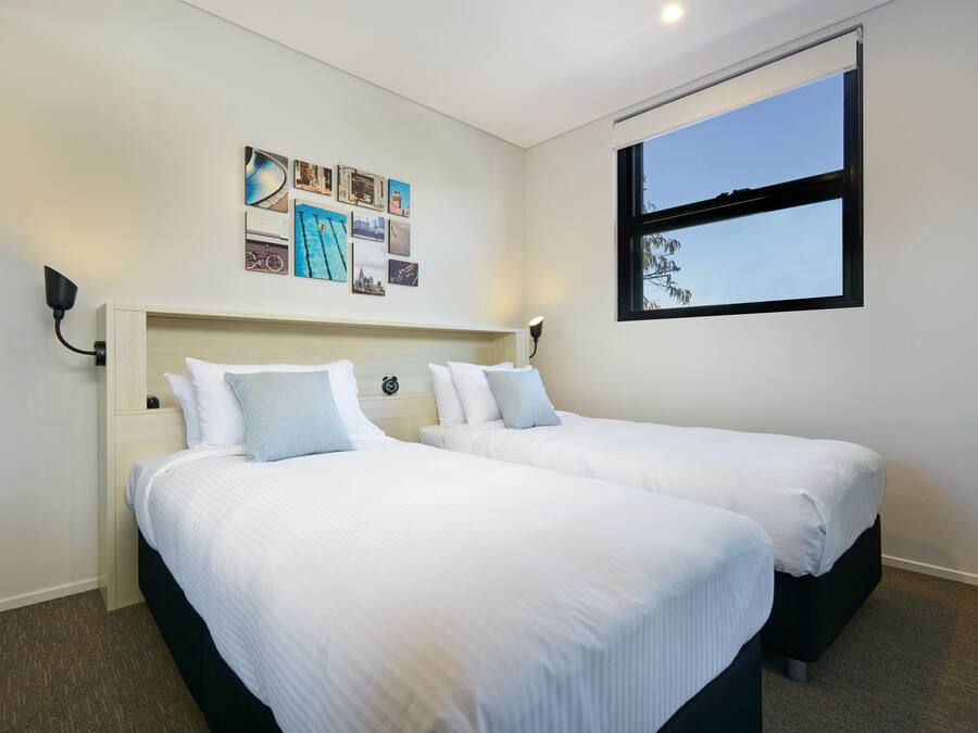 Quarto de hotel com duas camas, uma janela grande e obras de arte nas paredes.