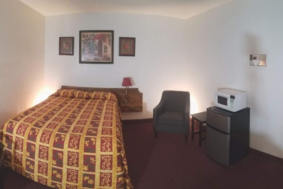 Quarto de hotel com cama, escrivaninha, cadeira, televisão e micro-ondas.