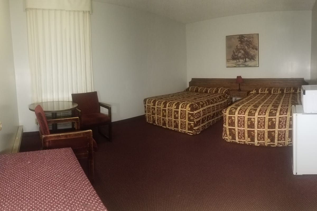Quarto de hotel com duas camas, uma mesa pequena com uma cadeira, um frigorífico e um quadro na parede.