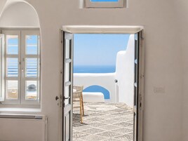 Uma porta que dá para uma varanda com vista para o mar, um chão estampado e uma parede branca.