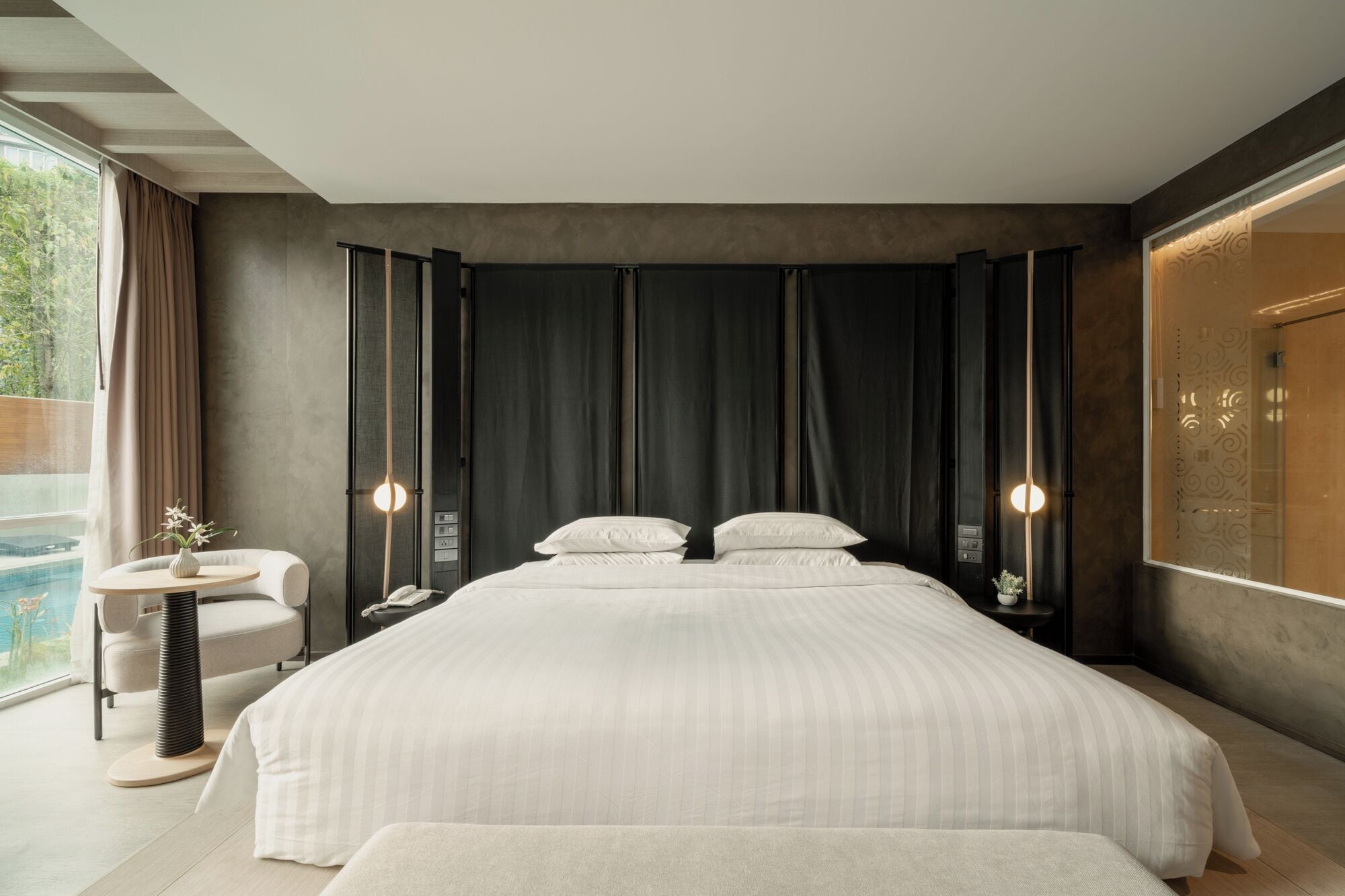 Quarto moderno com uma cama grande, uma mesinha redonda e vista para uma piscina.