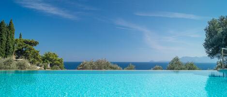 Piscina azul límpida com vista para o mar e montanhas ao longe.