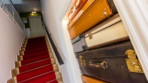 Uma escadaria com tapete vermelho que leva a um quarto cheio de malas empilhadas.