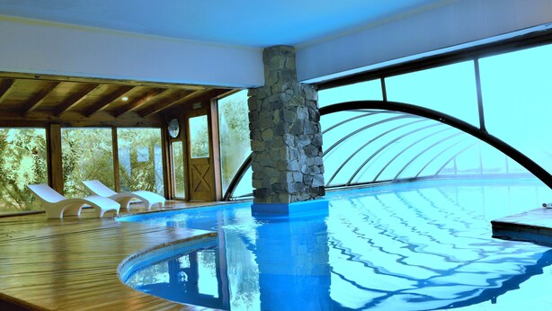 Piscina interna com um pilar de pedra, deck de madeira e cadeiras de descanso.