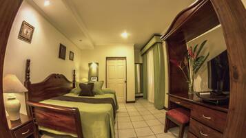 Quarto de hotel com cama de madeira, escrivaninha com gavetas, cadeira, luminária e espelho.
