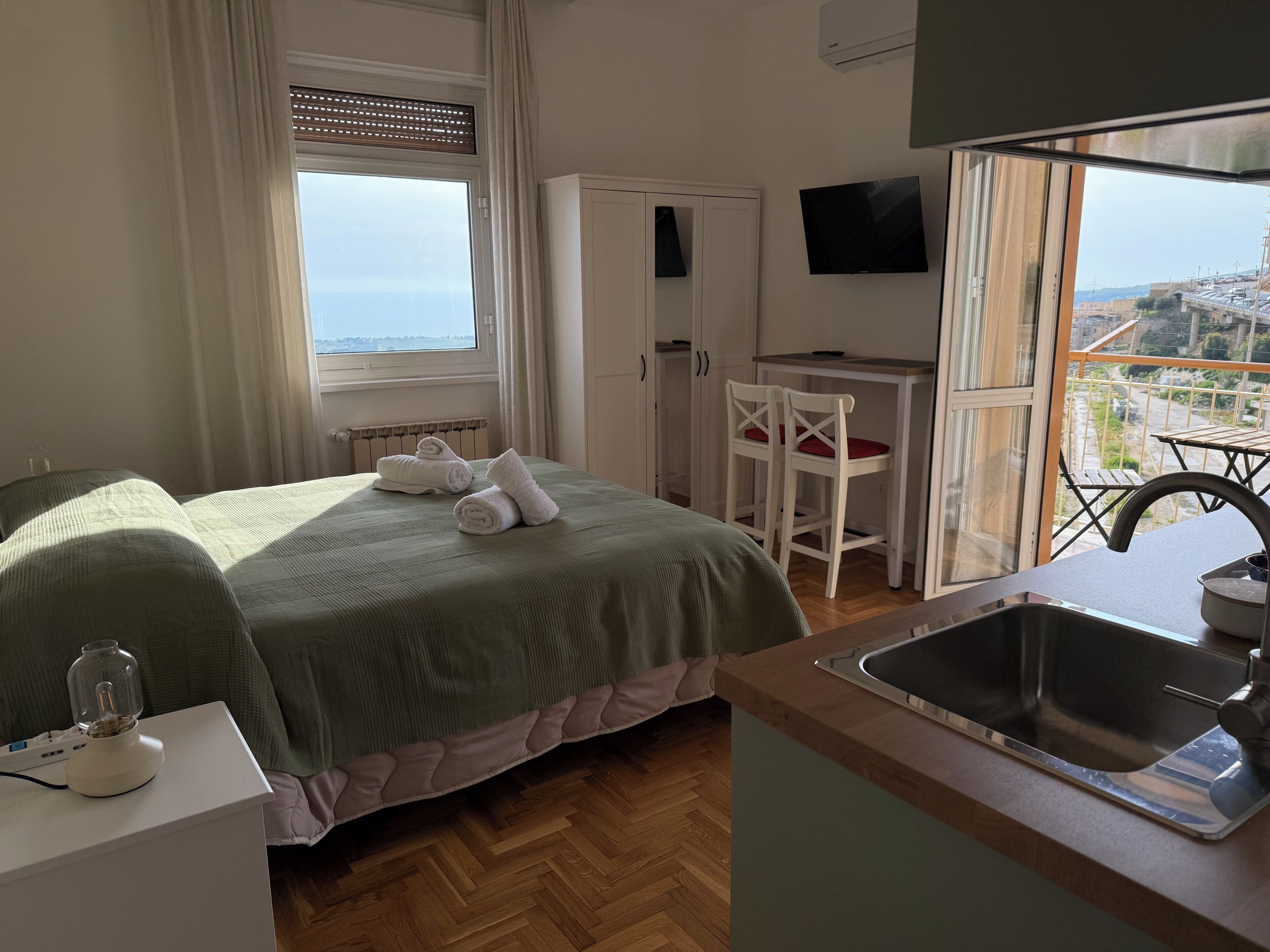 Quarto de hotel com cama, escrivaninha, cadeira, televisão e varanda com vista.