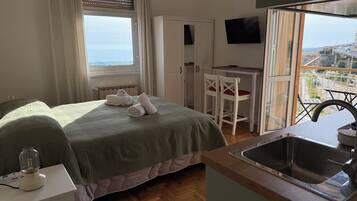 Quarto de hotel com cama, escrivaninha, cadeira, televisão e varanda com vista.