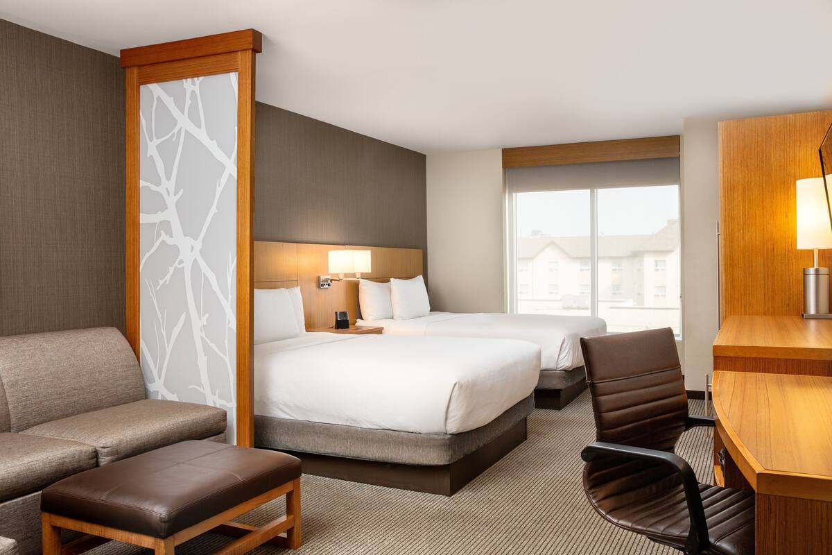 Quarto de hotel com duas camas, um sofá, uma mesa e uma cadeira.