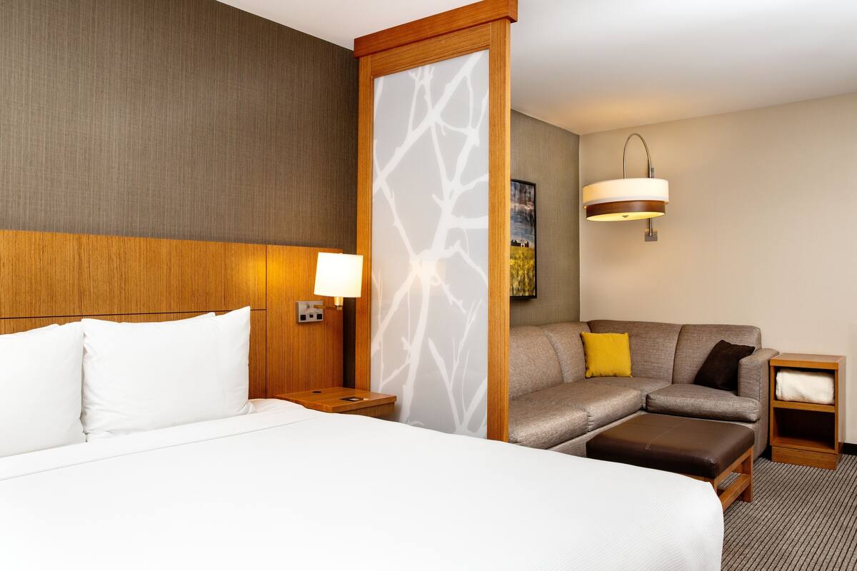Quarto de hotel com uma cama grande, um sofá, uma mesinha e uma mesa de cabeceira com abajur.