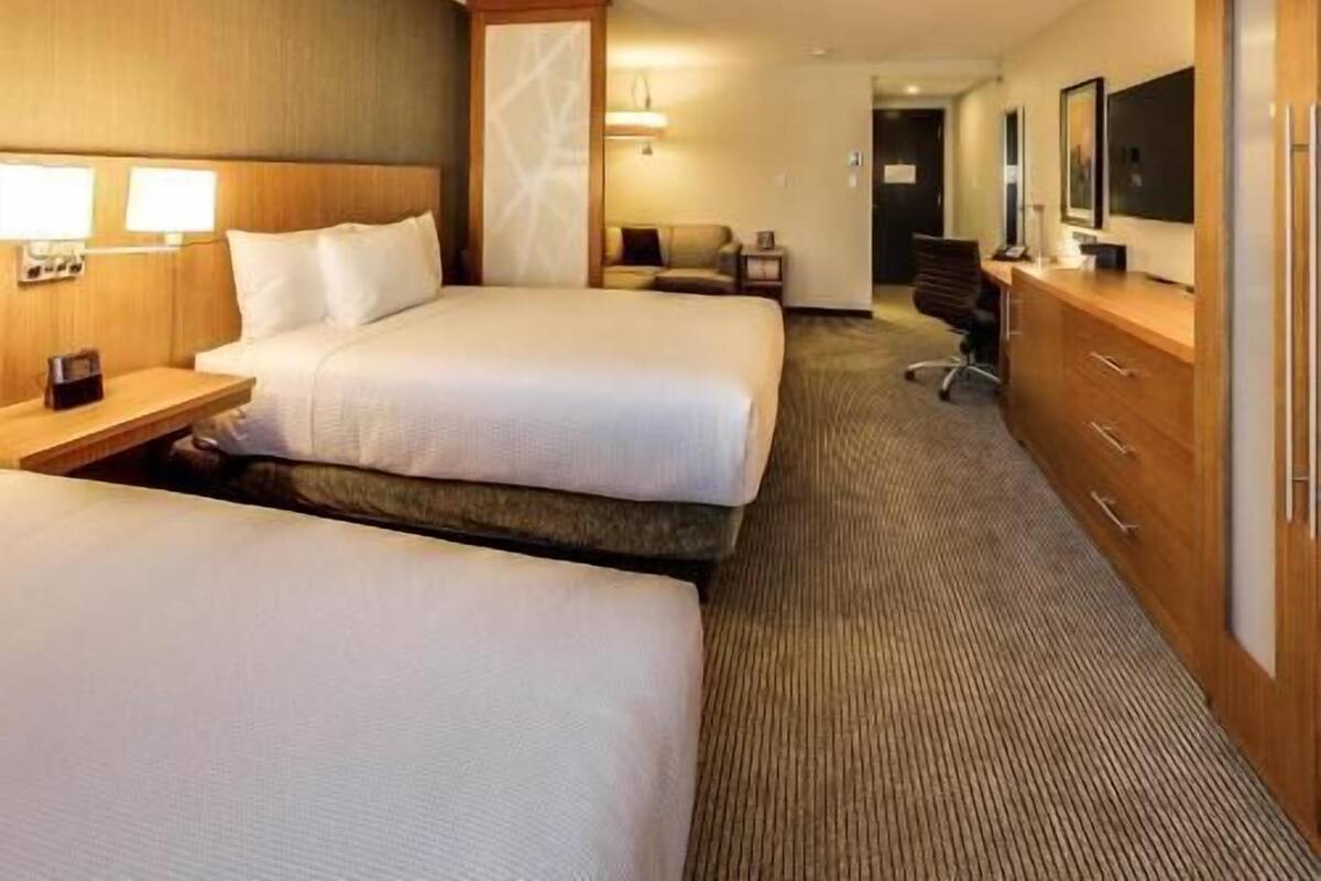 Quarto de hotel com duas camas, uma escrivaninha, uma cadeira, televisão e minibar.