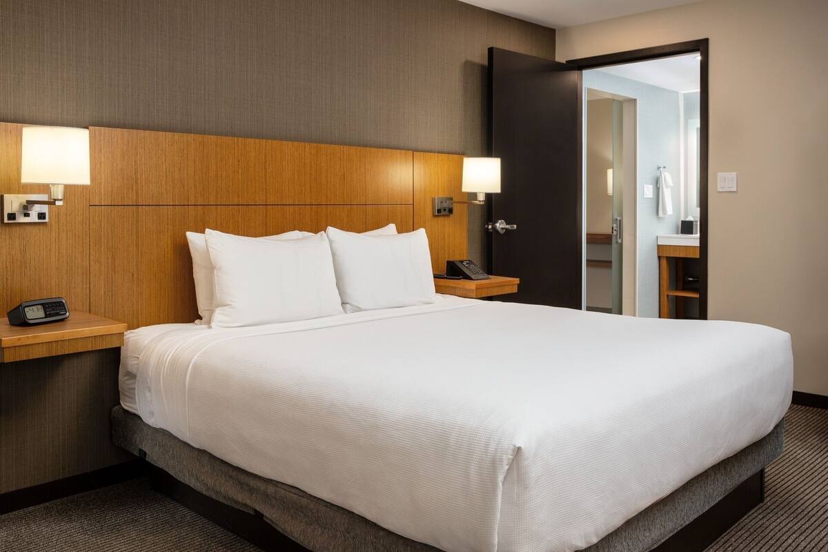 Quarto de hotel com uma cama grande, duas mesas de cabeceira com abajures, um telefone e um espelho.