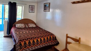 Quarto com cama de madeira, uma mesinha de madeira e janela com cortinas.