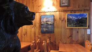 Interior em madeira com uma estátua de cachorro, bancos de madeira e quadros nas paredes.