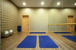 Quarto com piso de madeira, paredes espelhadas e colchonetes azuis para exercícios.