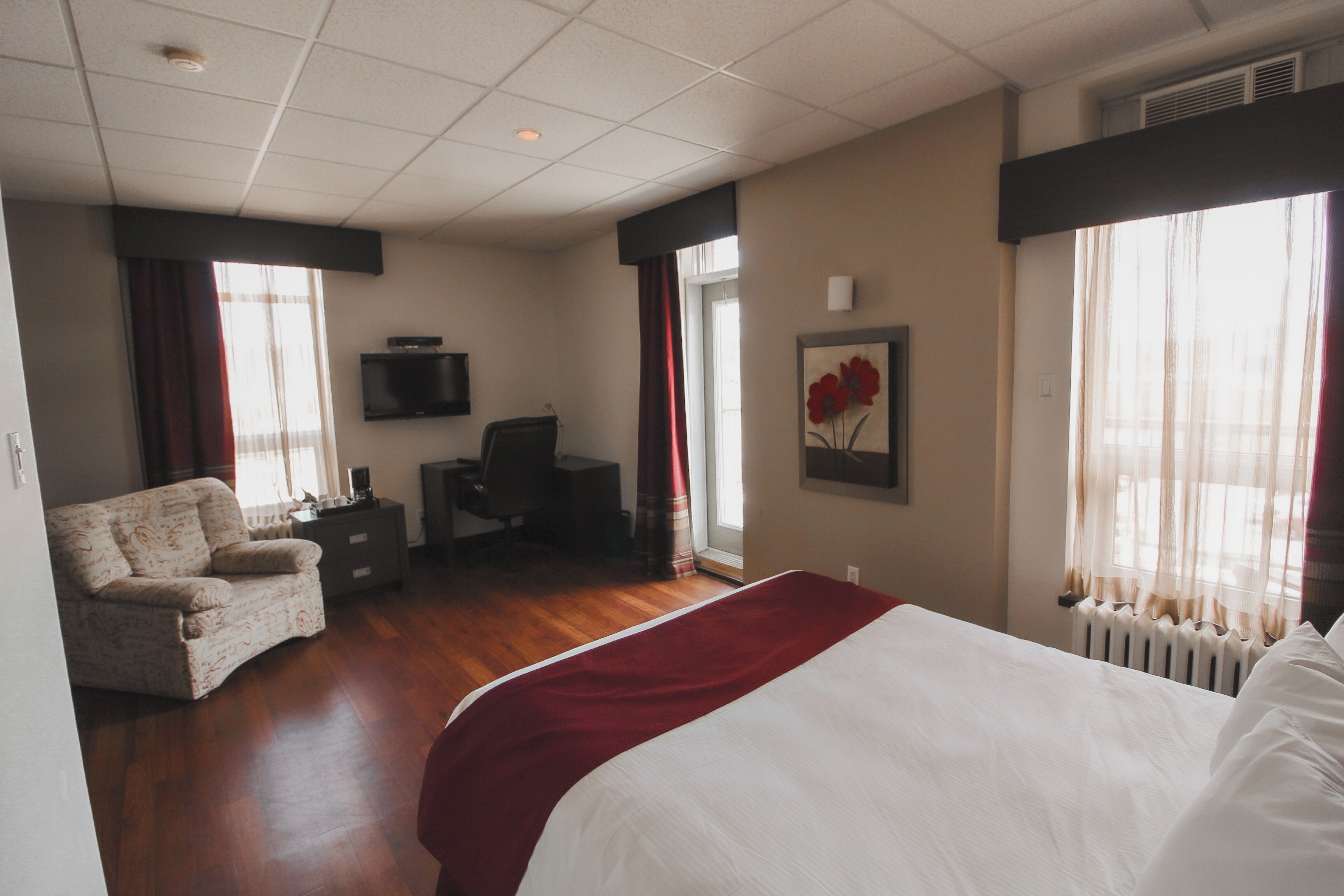 Quarto de hotel com cama, escrivaninha, cadeira, televisão e janela com cortinas.