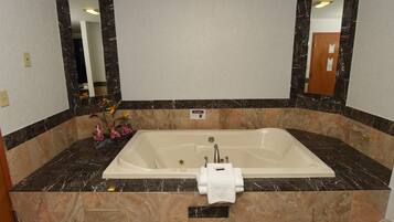 Uma banheira grande e retangular com interior branco, ladeada por dois espelhos com molduras de mármore preto, emoldurada por azulejos de mármore bege e preto.