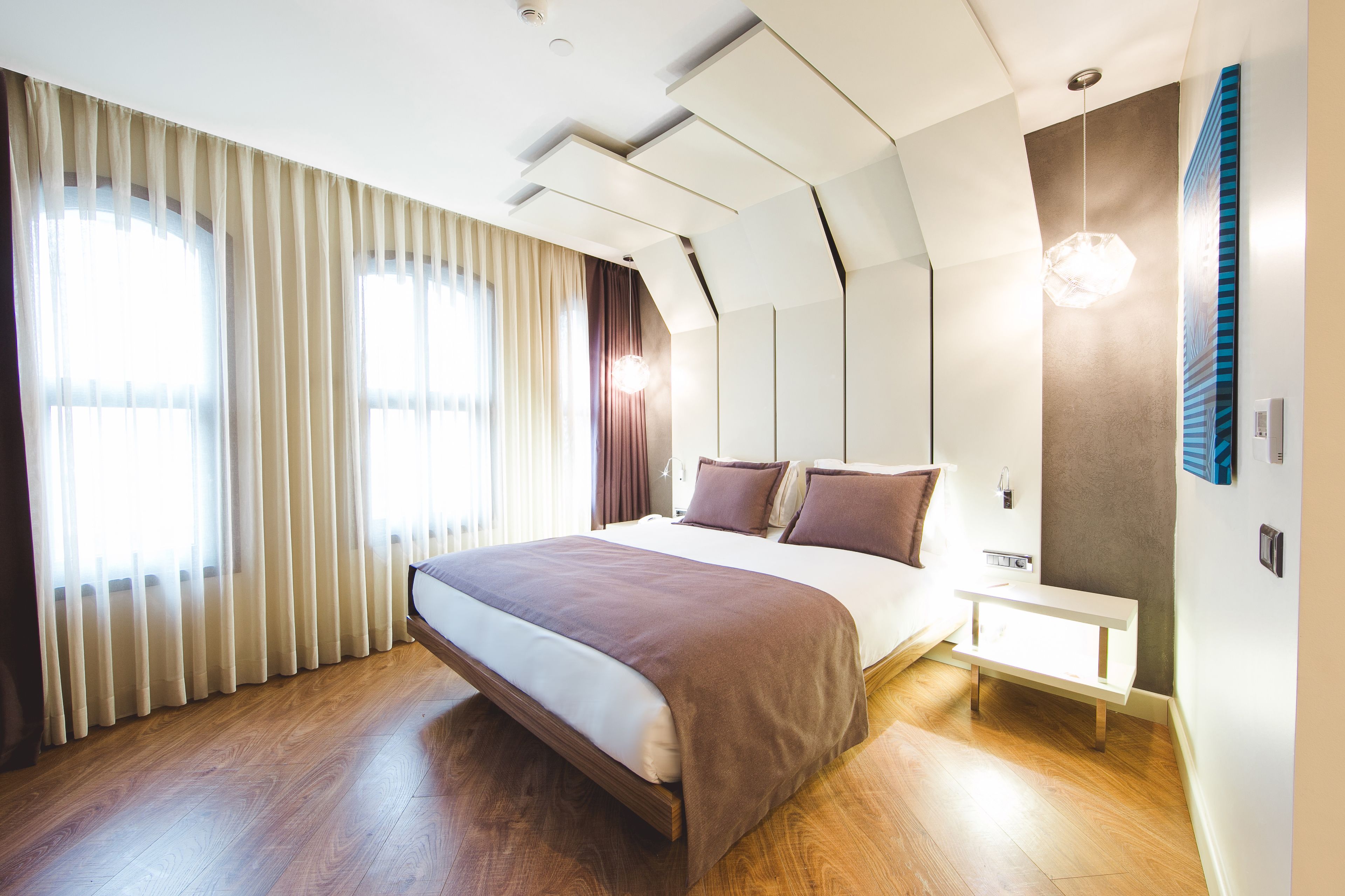 Quarto moderno com uma cama grande, piso de madeira e mesa de cabeceira.