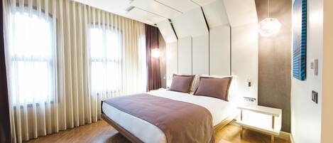 Quarto moderno com uma cama grande, piso de madeira e mesa de cabeceira.