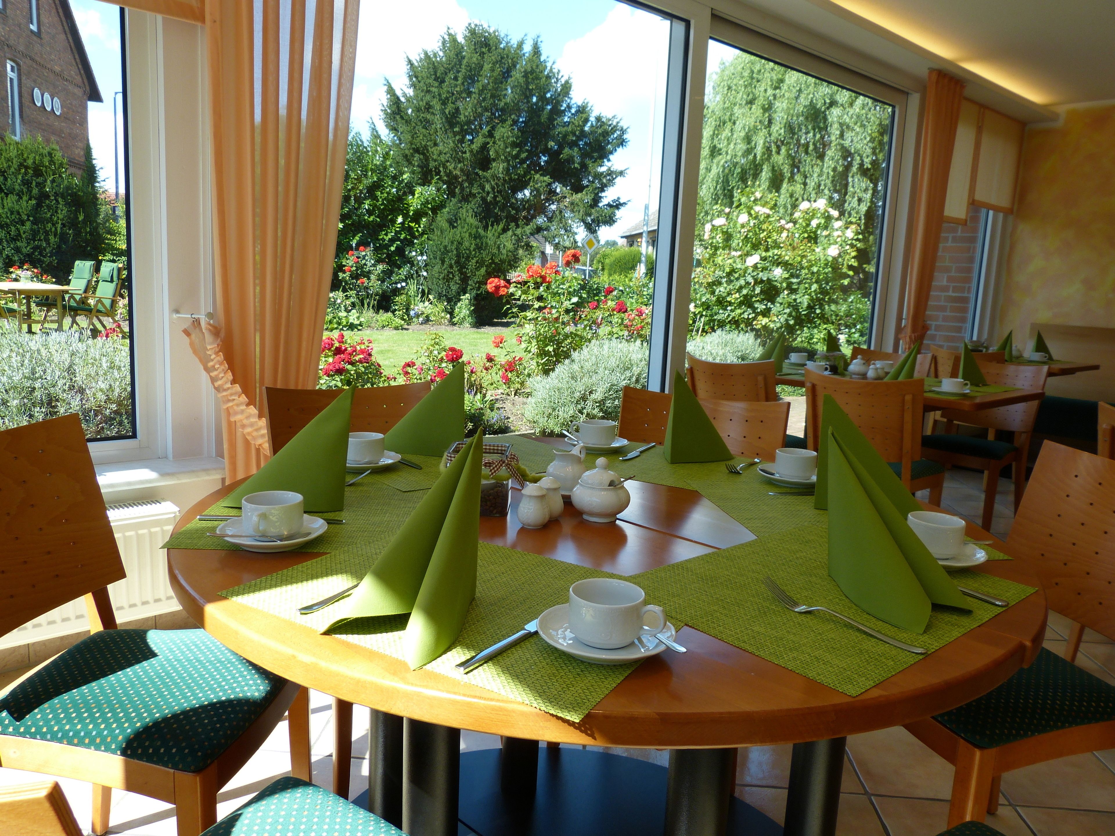 Uma sala de jantar com uma mesa redonda posta para quatro pessoas, rodeada por cadeiras com almofadas verdes.
