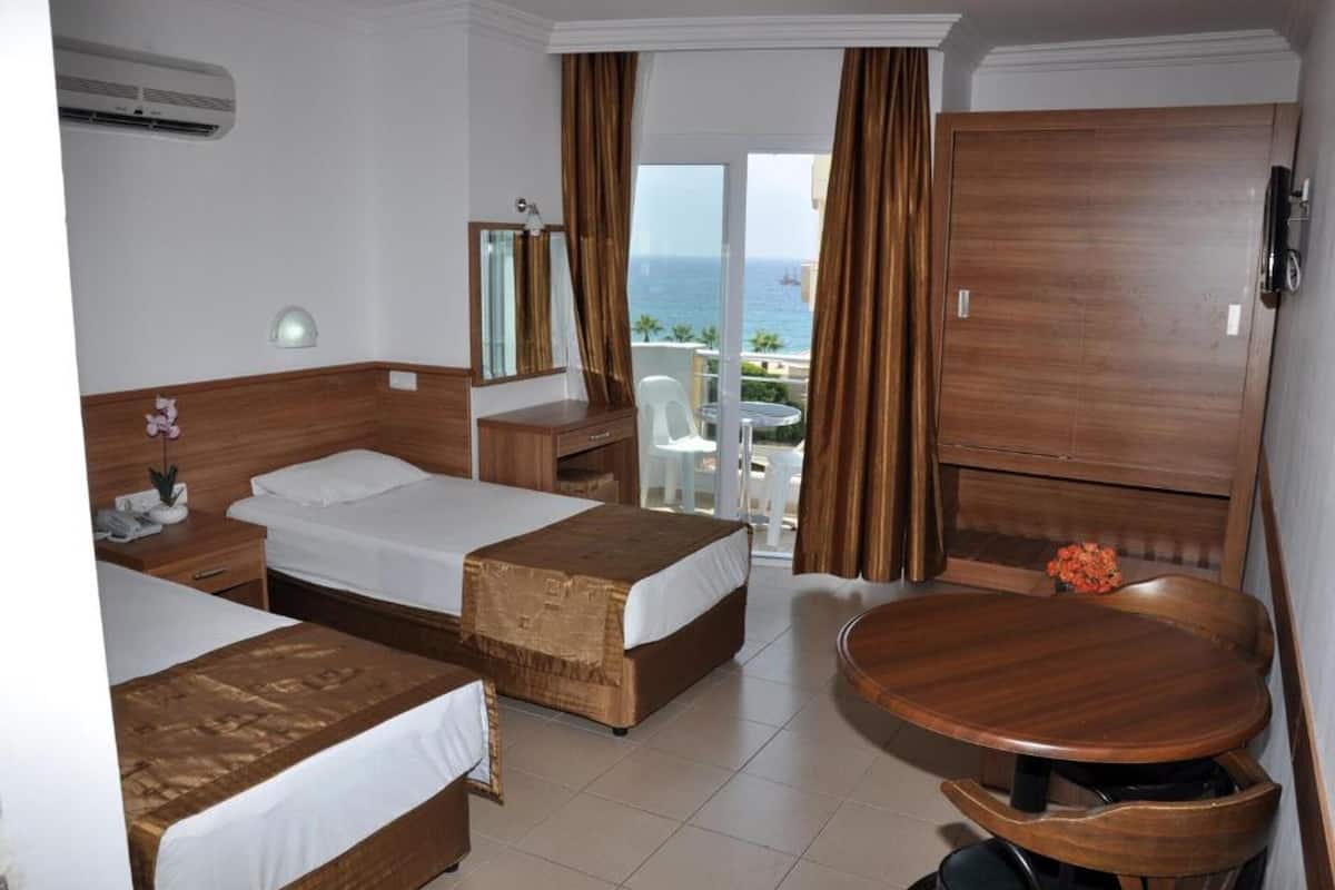 Quarto de hotel com duas camas, um guarda-roupa de madeira, uma mesa redonda e vista para o mar.