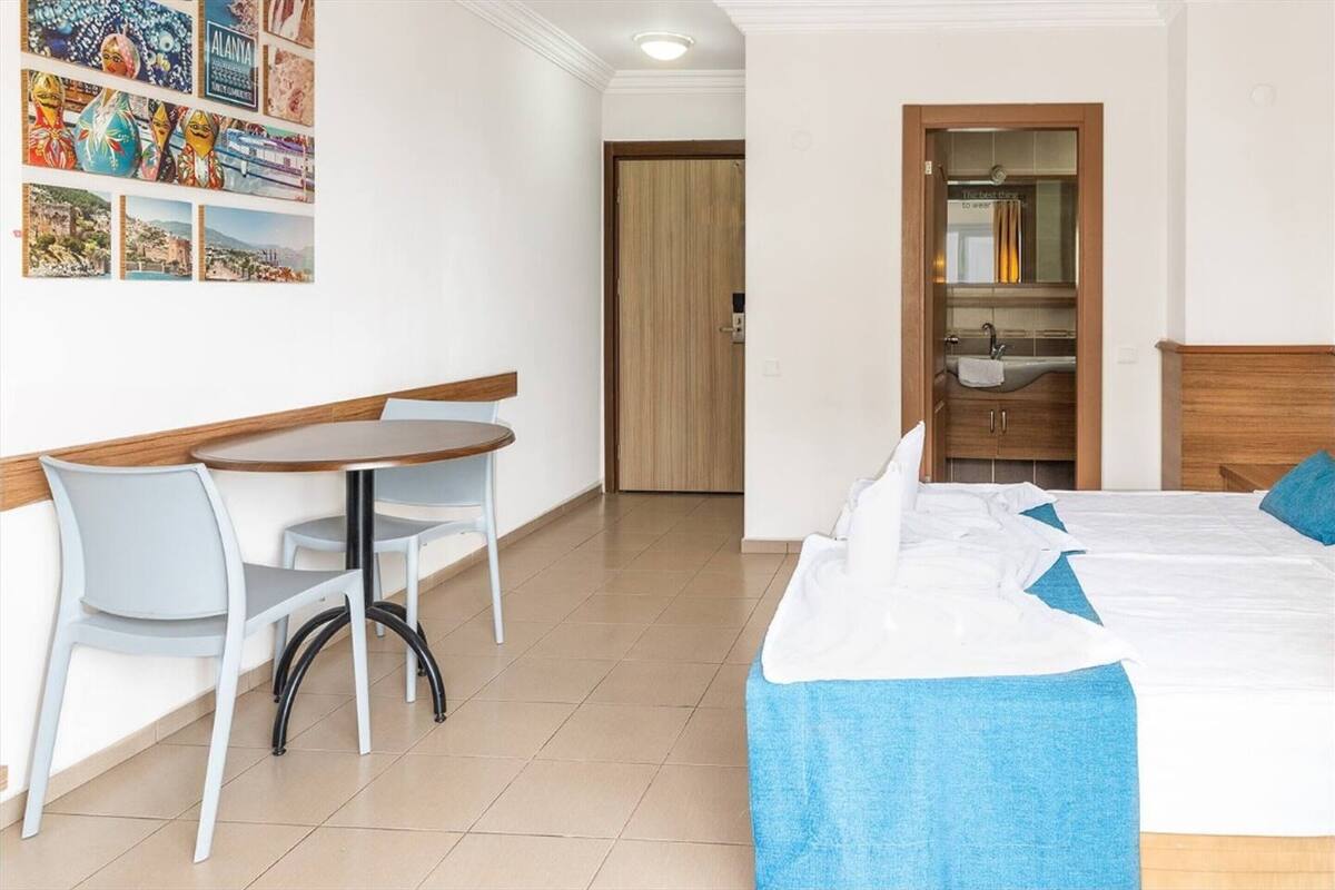 Quarto de hotel com uma cama, uma escrivaninha com cadeira, uma mesinha, um espelho e um banheiro com pia e armário.
