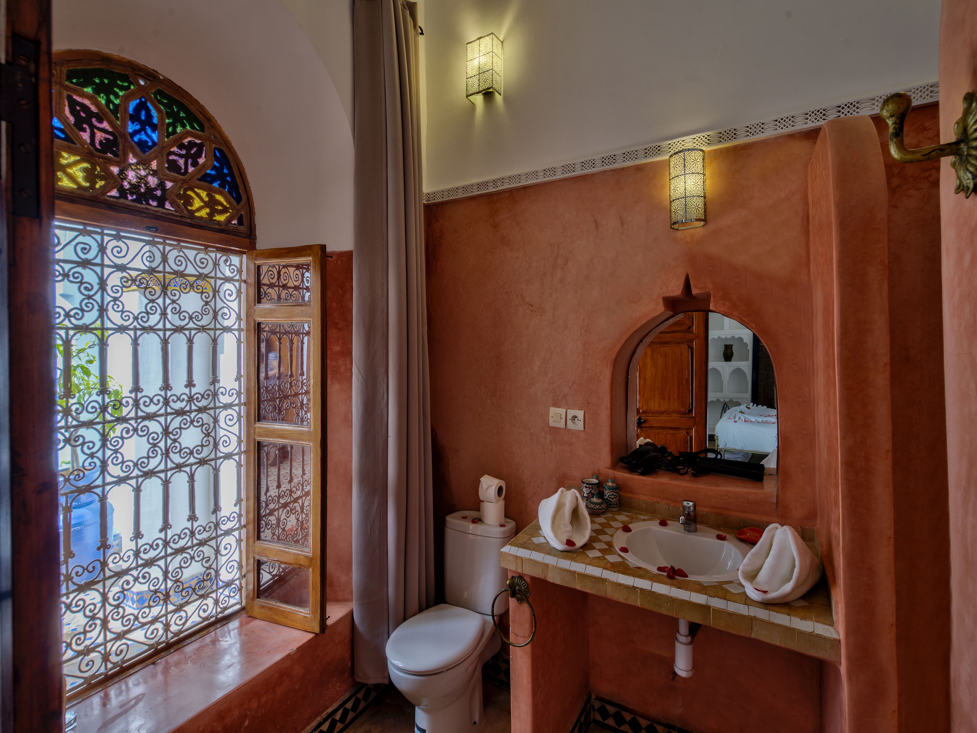 Uma casa de banho com um amplo vitral, uma pia com espelho e uma sanita.