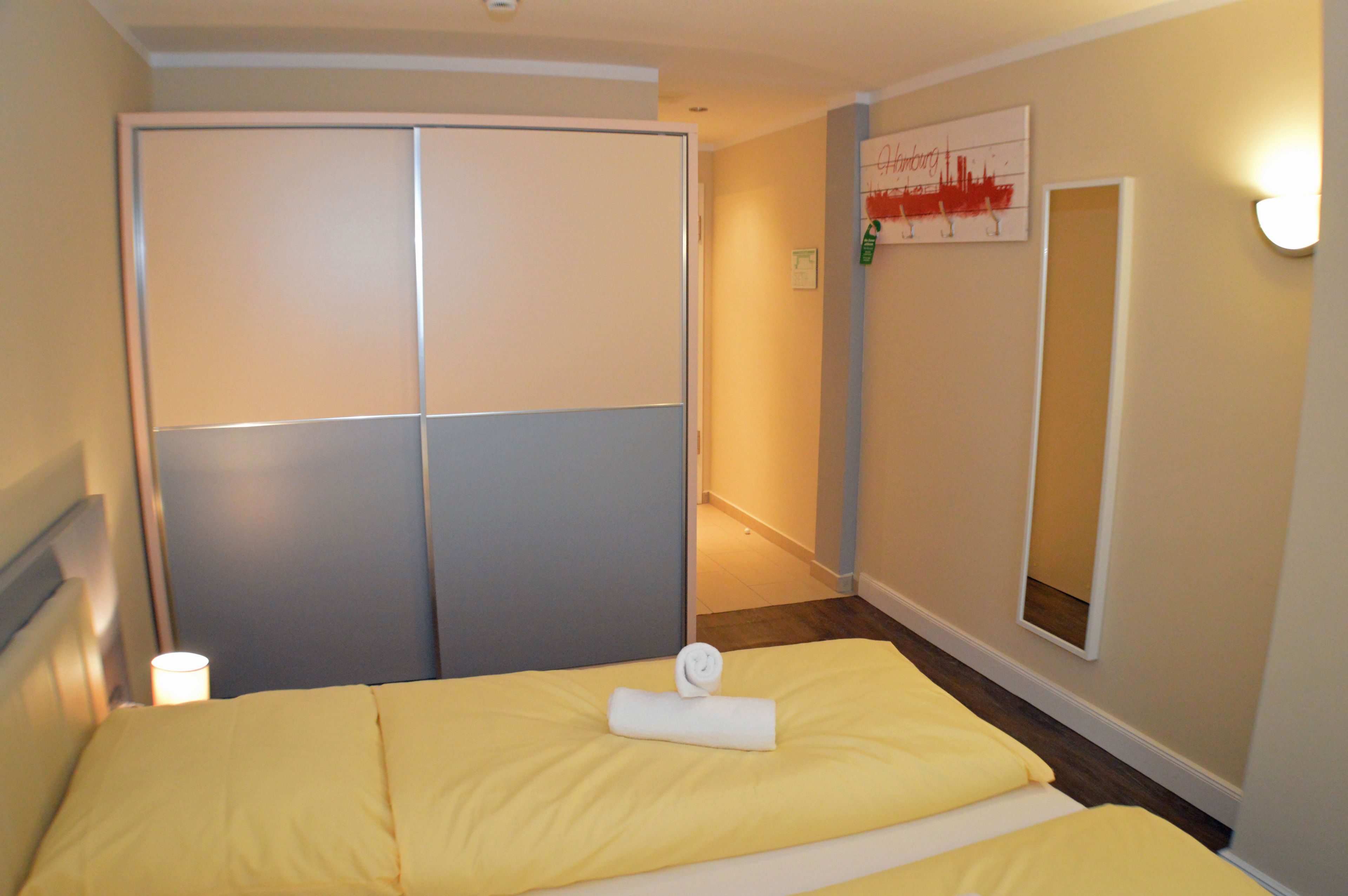 Quarto de hotel com cama, guarda-roupa, espelho e um quadro pendurado na parede.