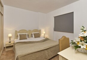 Quarto de hotel bem arrumado, com cama, mesas de cabeceira, uma cadeira e televisão fixada na parede.